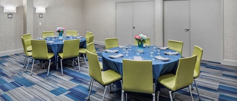 Uma sala de conferências com mesas redondas, cadeiras e centros de mesa com flores.