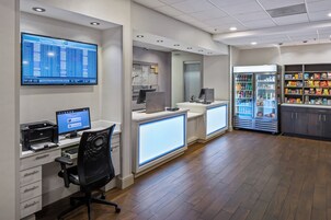 Área de check-in moderna em aeroporto, com painéis digitais, sinalização Holiday Inn Express e máquina de vendas automática.
