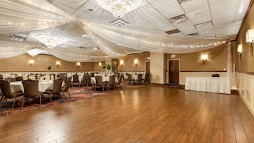 Uma sala de banquetes com mesas redondas, cadeiras, lustres e arandelas.