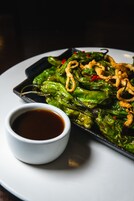 Uma travessa de pimentões grelhados com cebolas fritas e um pequeno recipiente com molho.