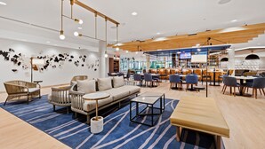 Um lobby de hotel moderno com área de estar central, um bar e um espaço para refeições.