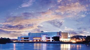 Hotel na orla marítima com vários edifícios, piscina refletora e horizonte urbano ao fundo.