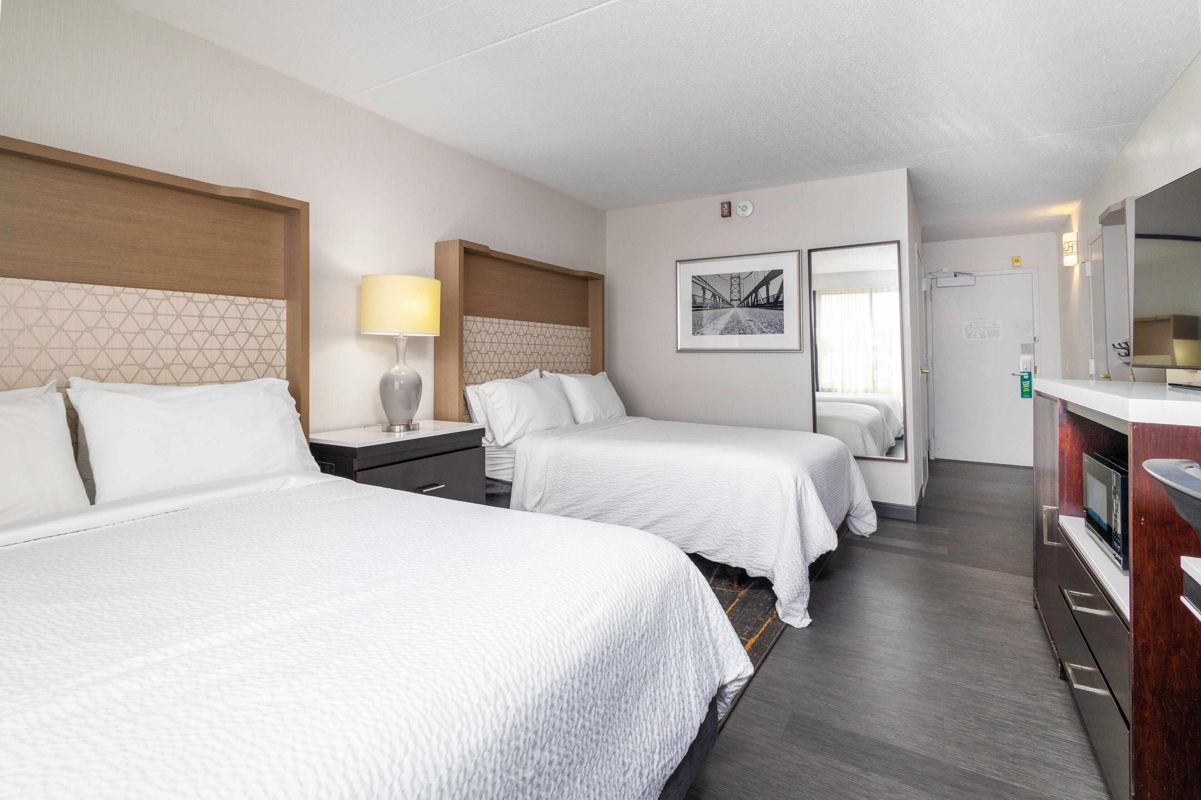 Quarto de hotel com duas camas, uma mesa de cabeceira com abajur, um quadro na parede e um micro-ondas no canto.