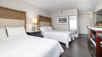 Quarto de hotel com duas camas, uma mesa de cabeceira com abajur, um quadro na parede e um micro-ondas no canto.