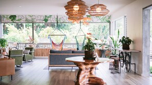 Uma sala de estar ampla com uma mesa de centro de madeira, um sofá e uma rede. Há luminárias de vime penduradas no teto e uma grande janela com vista para o verde lá fora.