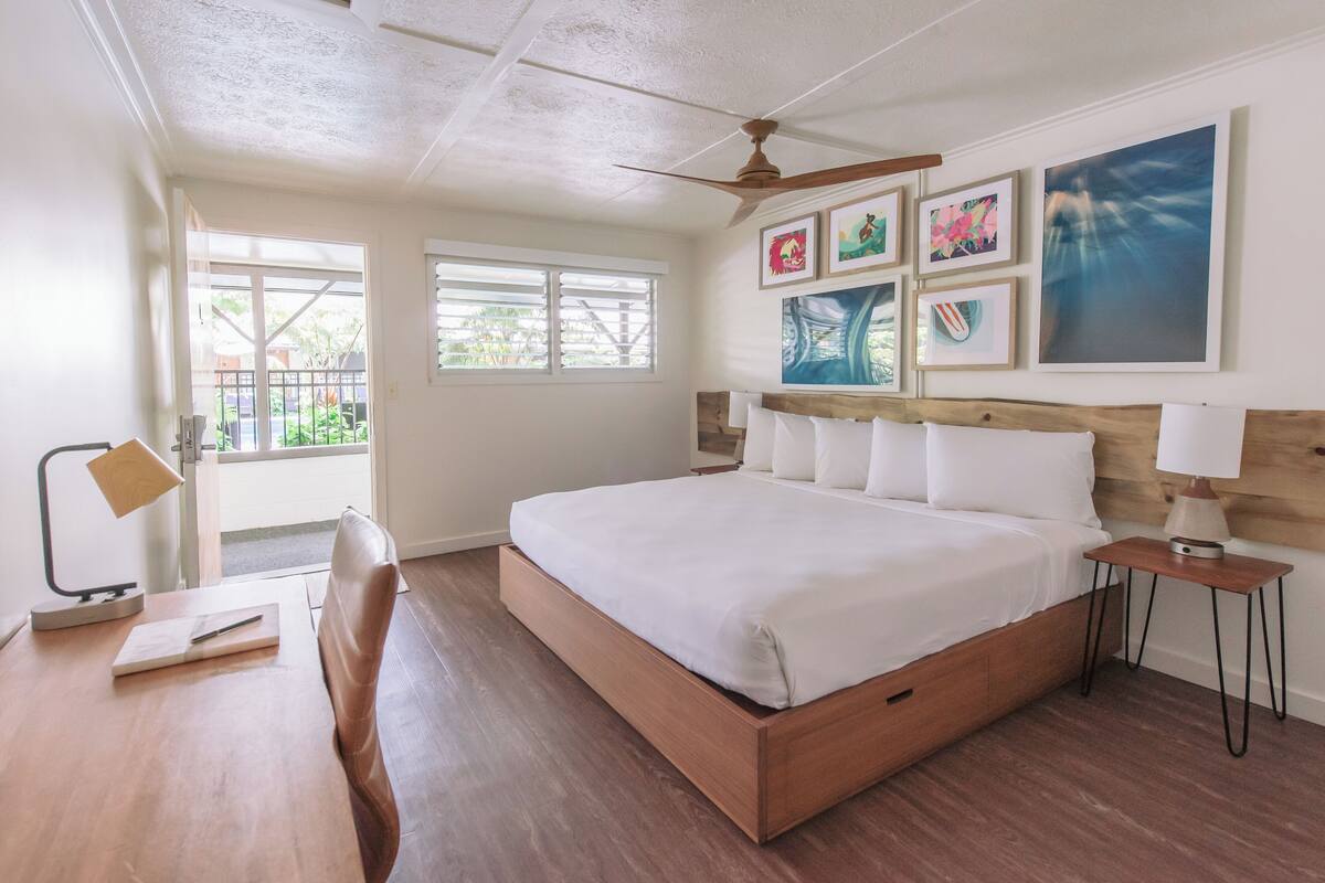 Quarto com cama de madeira, escrivaninha com luminária e obras de arte nas paredes.