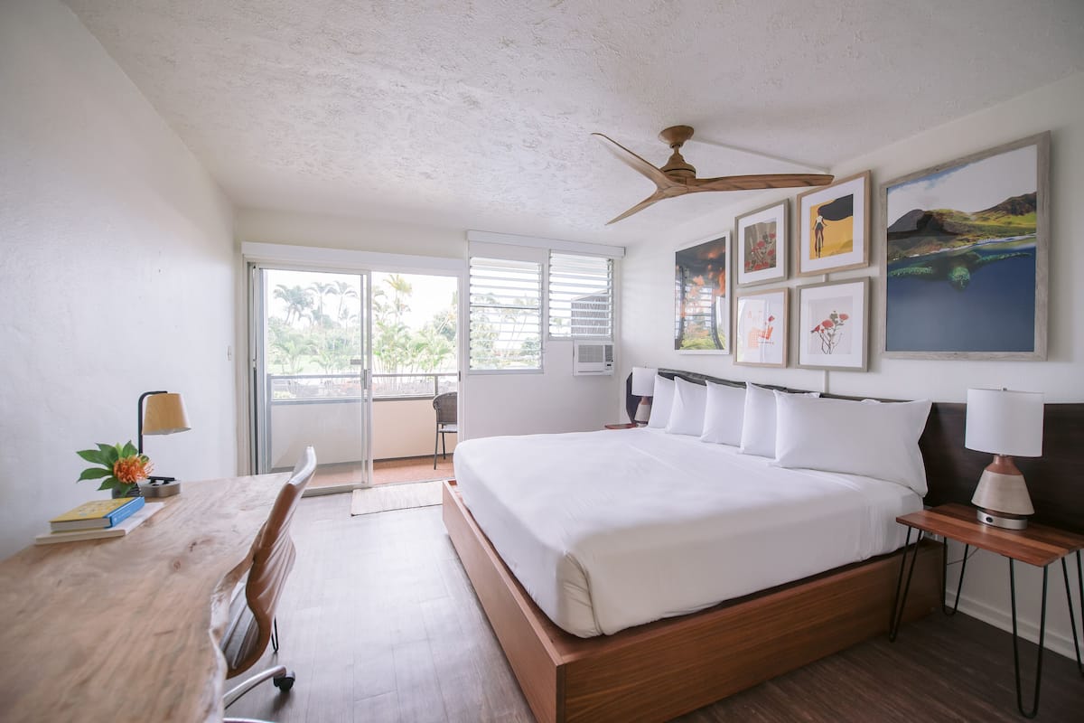 Quarto com uma cama grande, uma escrivaninha com cadeira, um ventilador de teto e obras de arte na parede.
