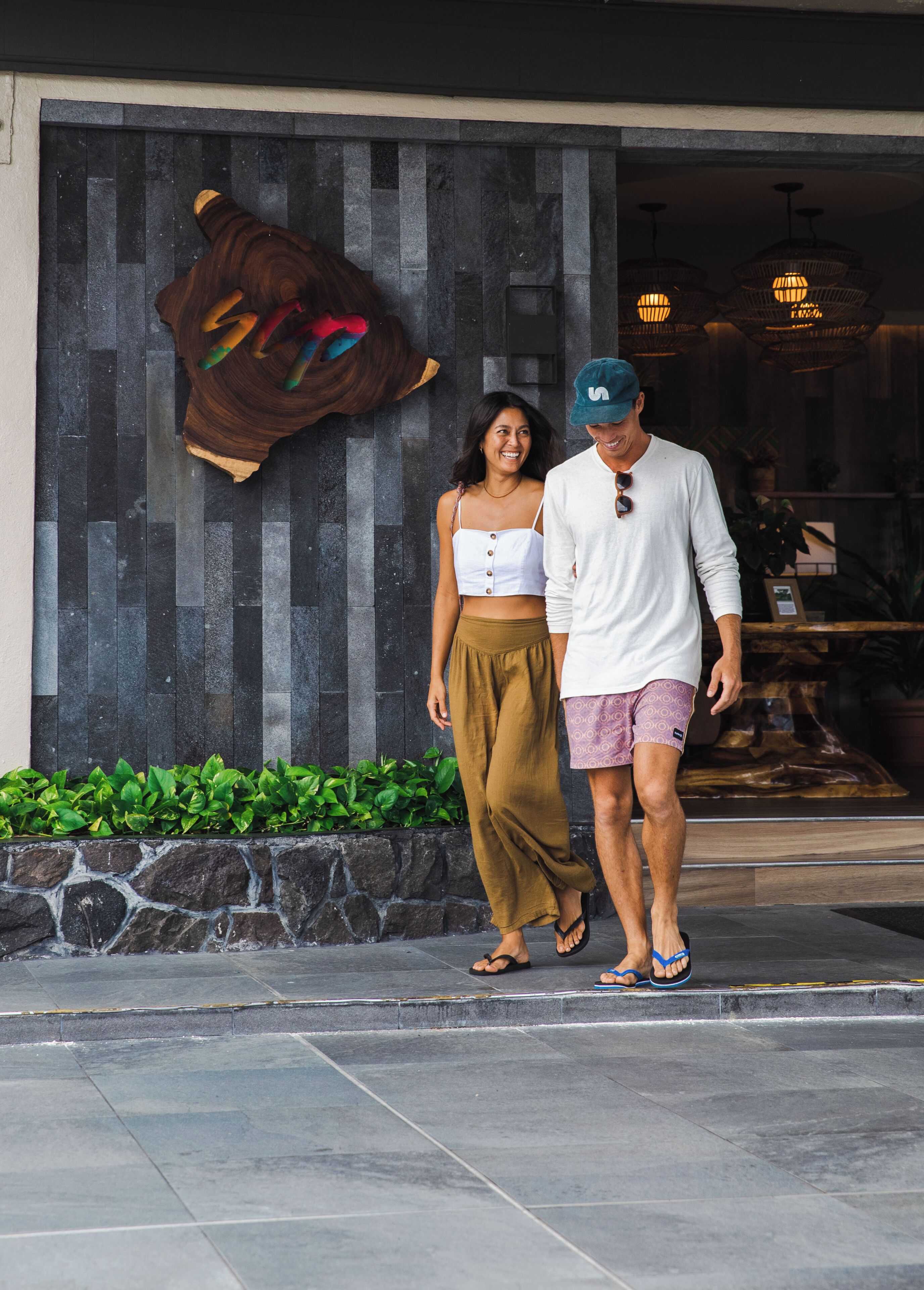 Um casal caminhando em frente a um edifício com parede de pedra e um detalhe de madeira pendurado.