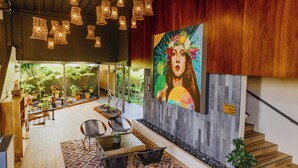Um espaço amplo e interno com escada, teto de madeira, luminárias pendentes, um mural, plantas em vasos e uma área de estar.