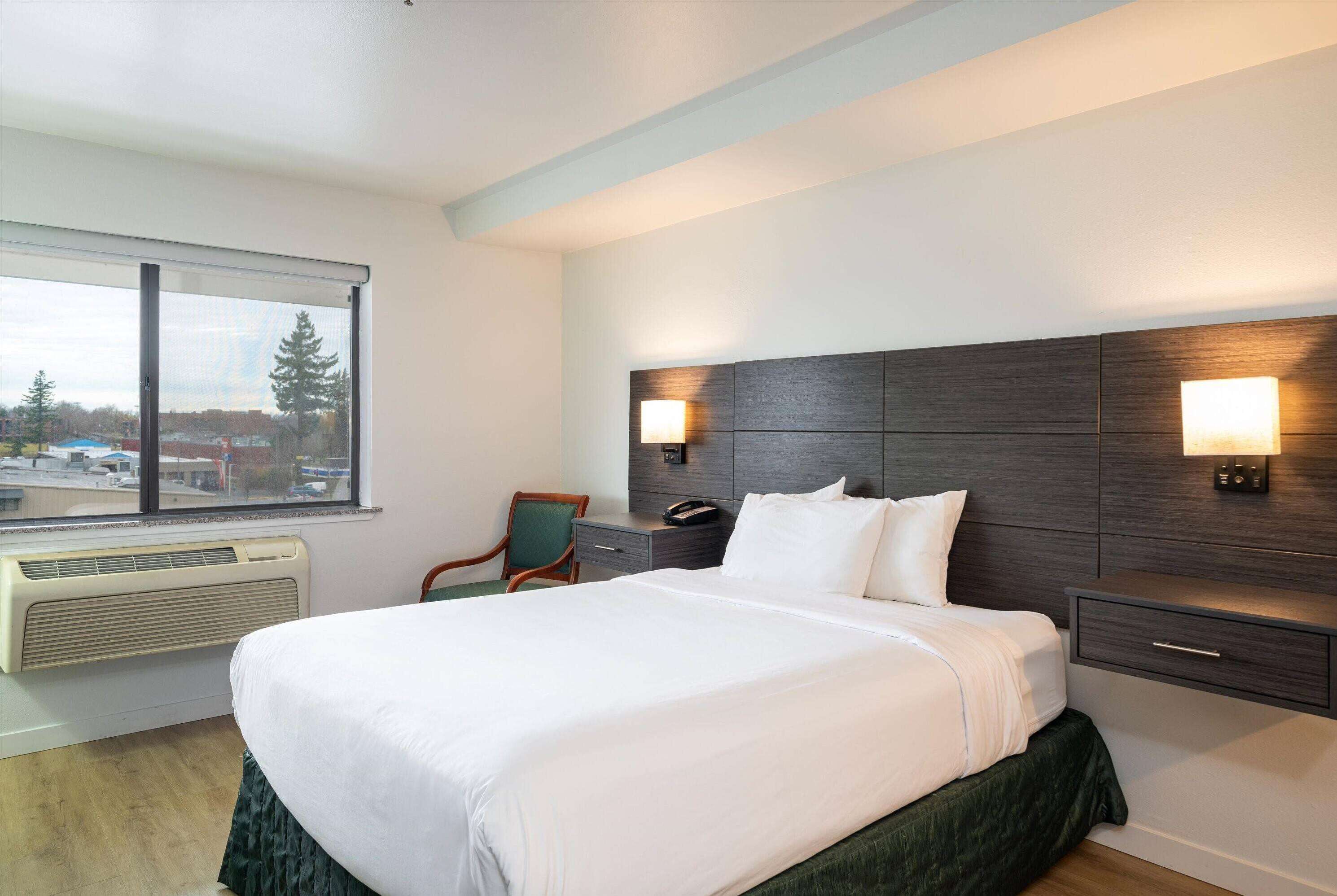 Quarto de hotel com uma cama grande, uma mesa com cadeira, uma janela com vista para o exterior e uma luminária na parede.