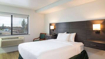 Quarto de hotel com uma cama grande, uma mesa com cadeira, uma janela com vista para o exterior e uma luminária na parede.