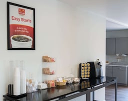 Uma área de cozinha com estação de café, incluindo cafeteira, xícaras e sachês de café.