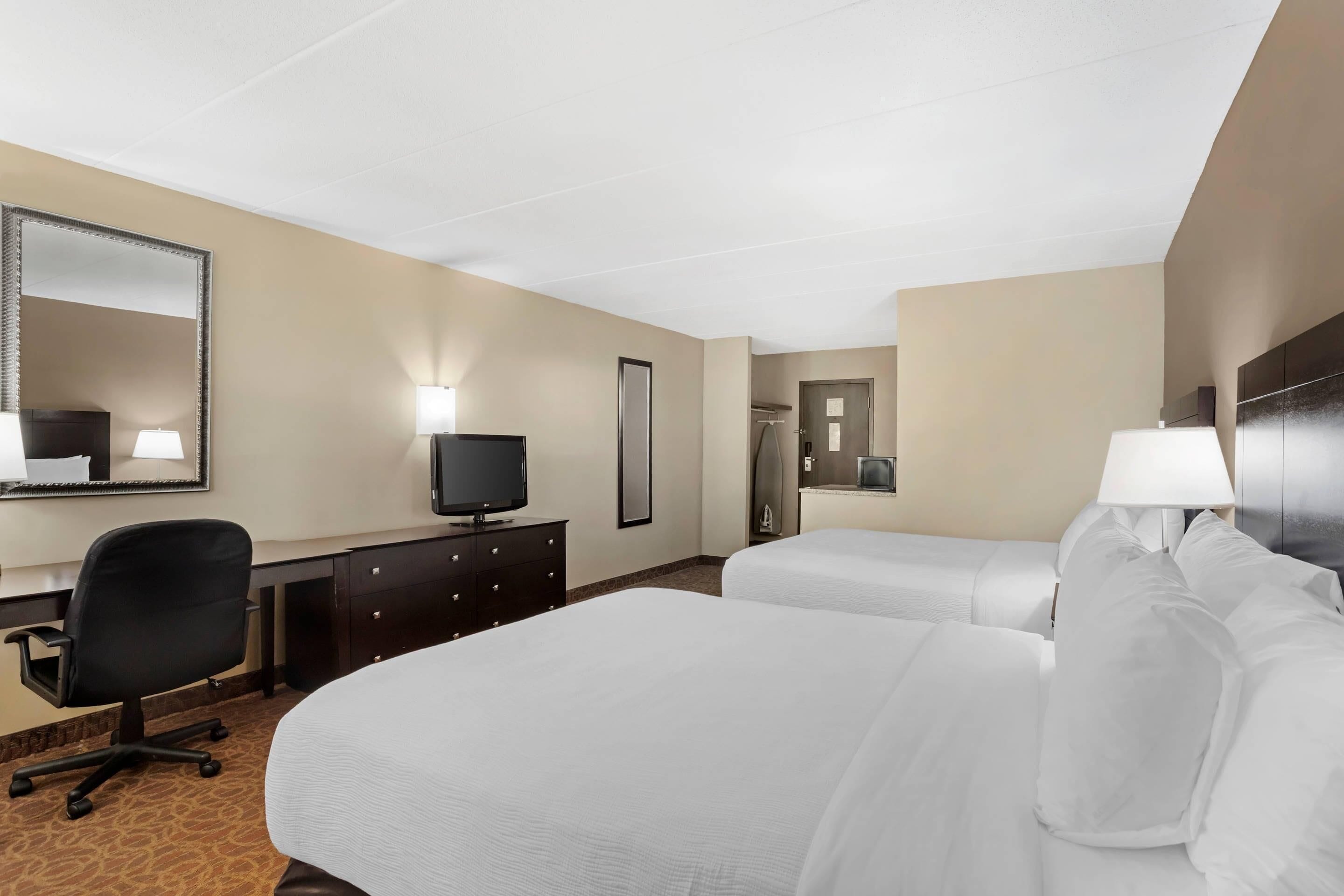 Quarto de hotel com duas camas, uma mesa de trabalho com cadeira, televisão e espelho.