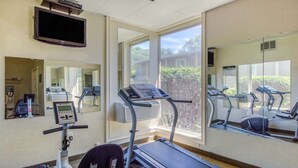 Academia com esteira, bicicleta ergométrica e parede espelhada refletindo equipamentos de ginástica.
