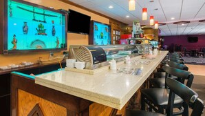 Uma área de buffet com um balcão extenso, várias cadeiras e uma vitrine com diversos itens.