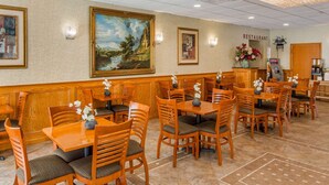 Restaurante com mesas e cadeiras de madeira, um quadro grande na parede e uma placa indicando a área do restaurante.
