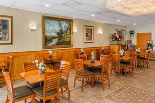 Restaurante com mesas e cadeiras de madeira, um quadro grande na parede e uma placa indicando a área do restaurante.