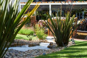 Um caminho de jardim com pedras e plantas, área de estar ao ar livre e um edifício com varanda coberta.