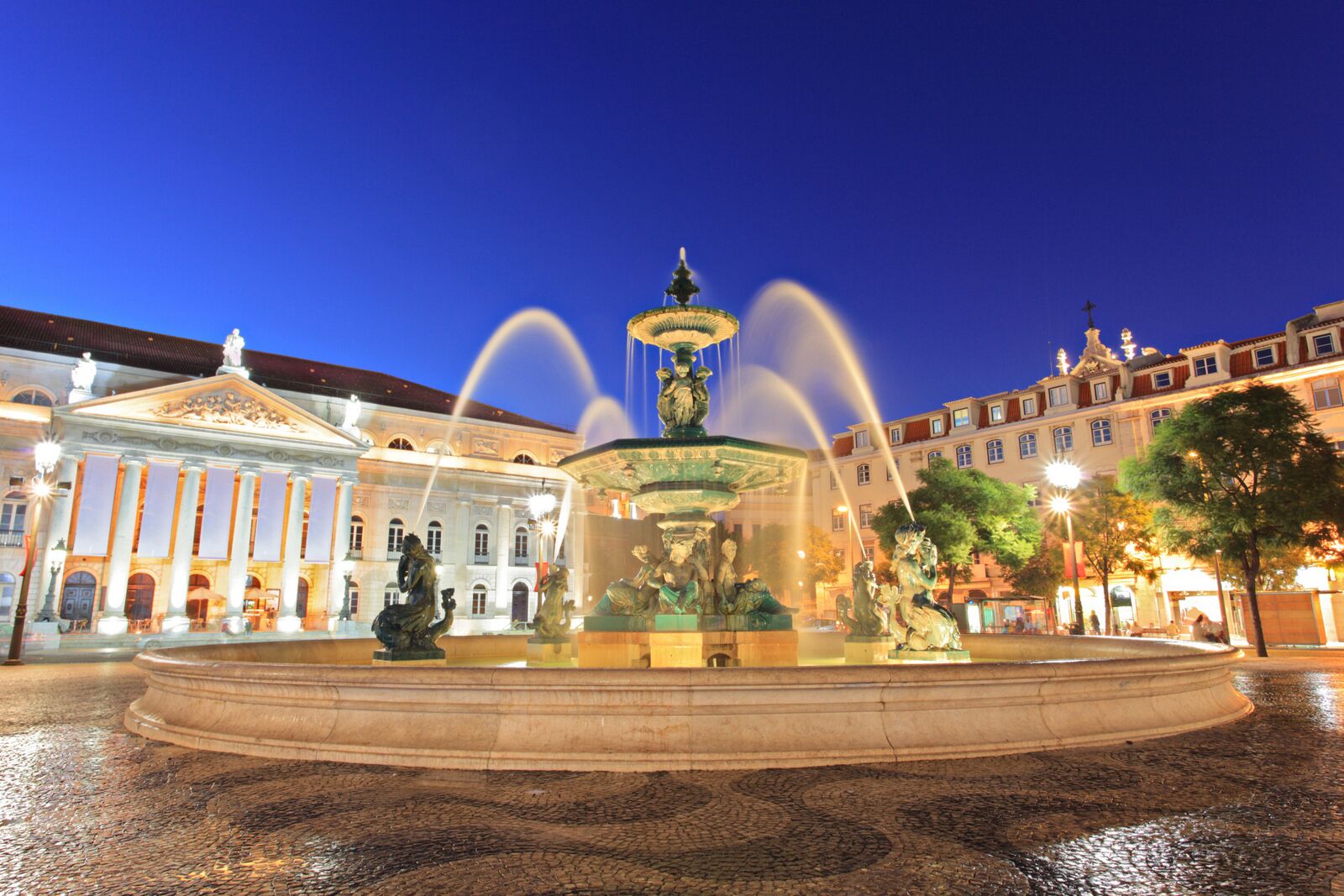 Uma fonte histórica com vários jatos de água numa praça rodeada por arquitetura clássica.