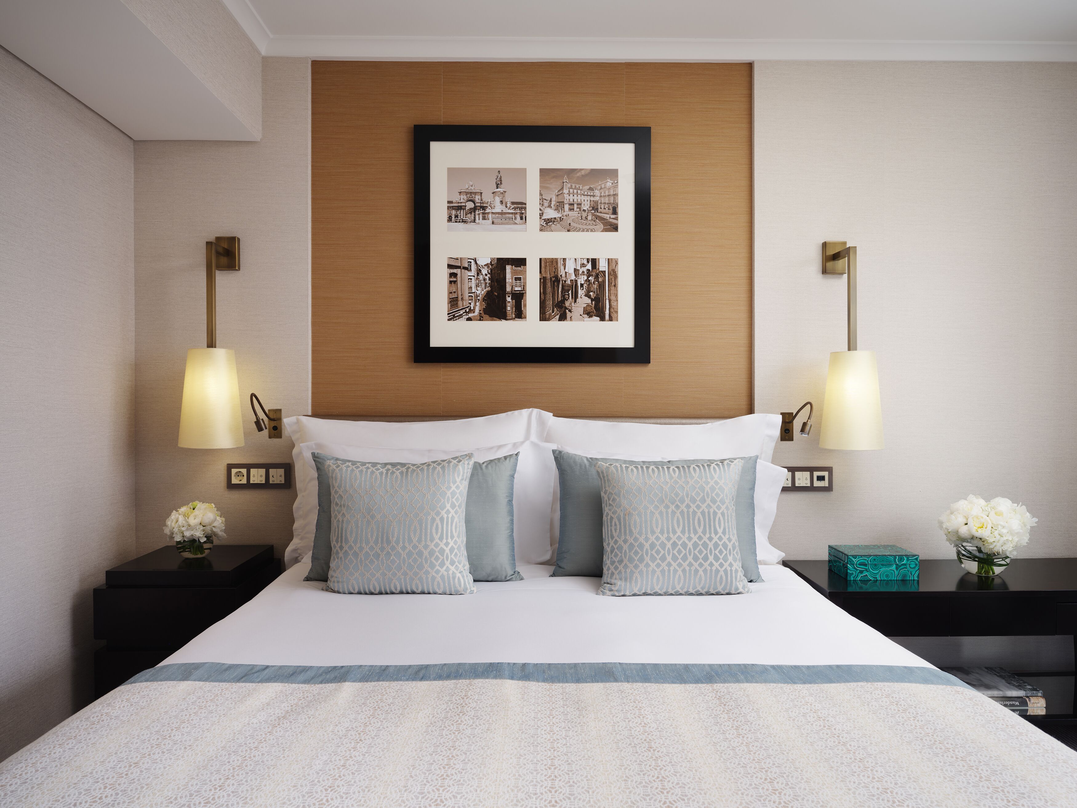 Quarto de hotel com uma cama grande, duas mesas de cabeceira, uma fotografia emoldurada na parede e duas luminárias fixadas na parede.