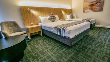 Quarto de hotel com uma cama grande, duas mesas de cabeceira, uma cadeira e um tapete verde.