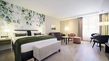 Quarto de hotel com cama, escrivaninha, cadeira, sofá e parede com padrão de folhas.