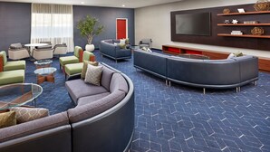 Um hall de hotel moderno com um sofá curvo, mesas redondas e uma televisão de tela plana na parede.