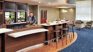 Uma área de bar moderna com balcão de madeira, banquetas e uma televisão acima.