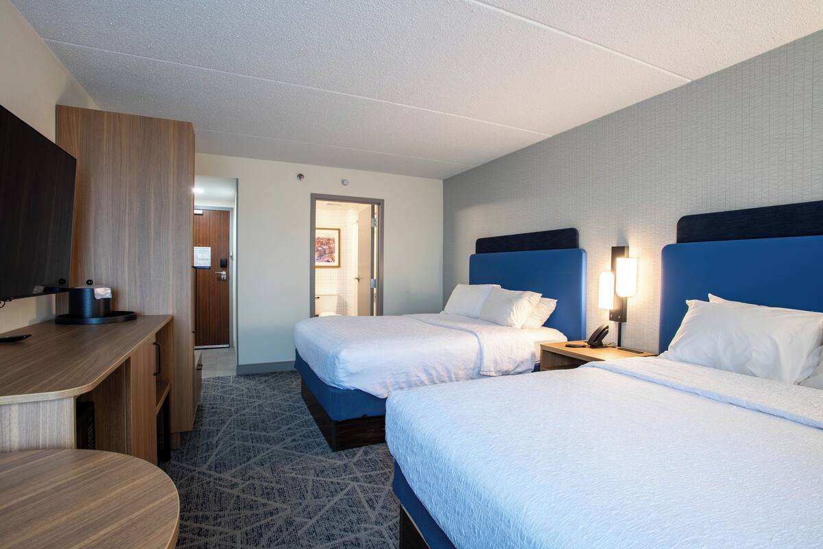 Quarto de hotel com duas camas, uma escrivaninha e uma televisão.