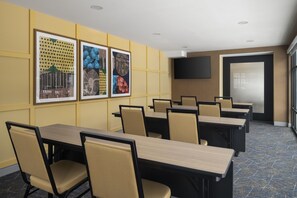 Sala de conferência com mesas, cadeiras, TV de tela plana e quadros nas paredes.