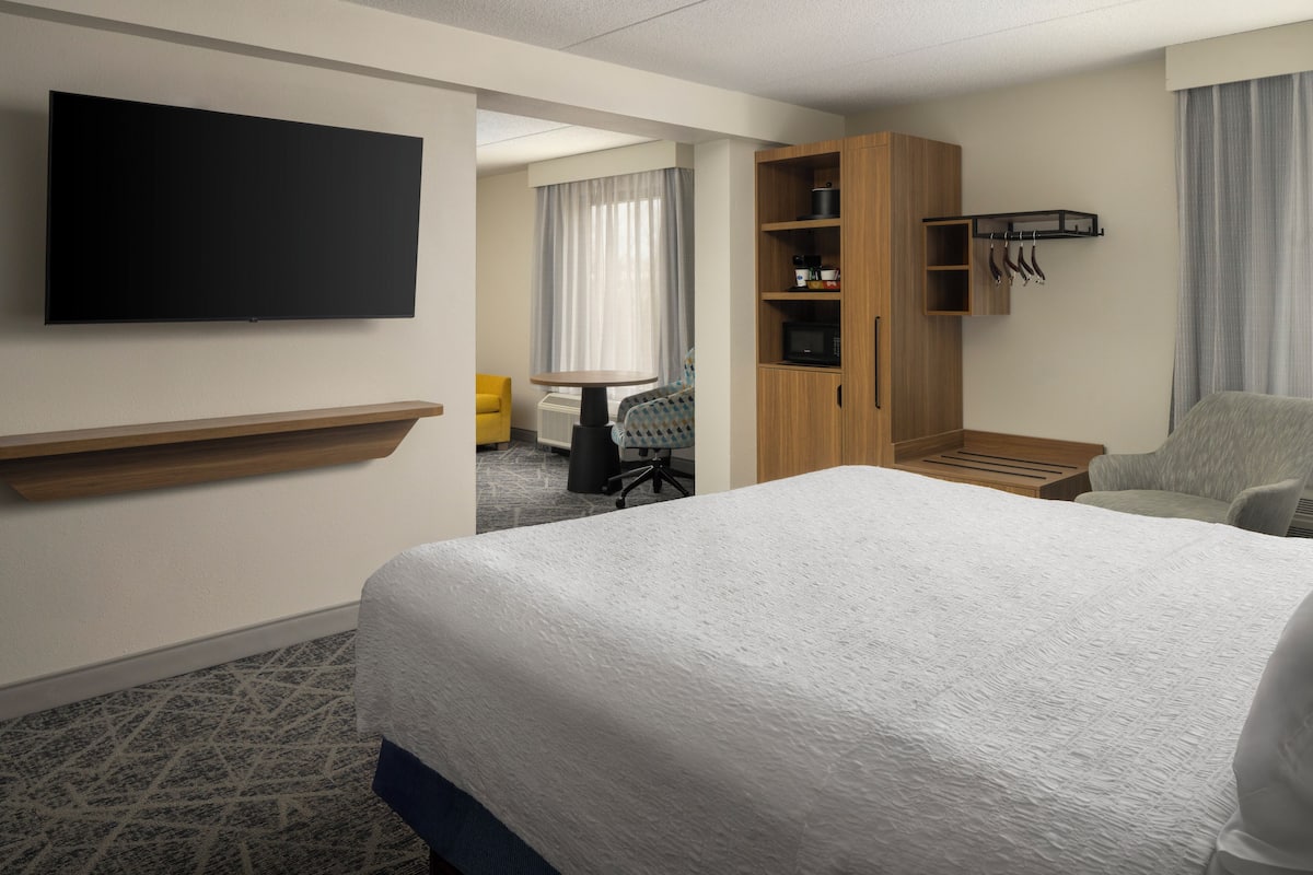 Quarto de hotel com uma cama grande, televisão de tela plana na parede, armário de madeira, mesa pequena e uma cadeira.