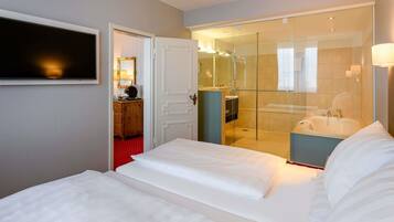 Quarto de hotel com cama, televisão, banheiro com chuveiro e espelho.