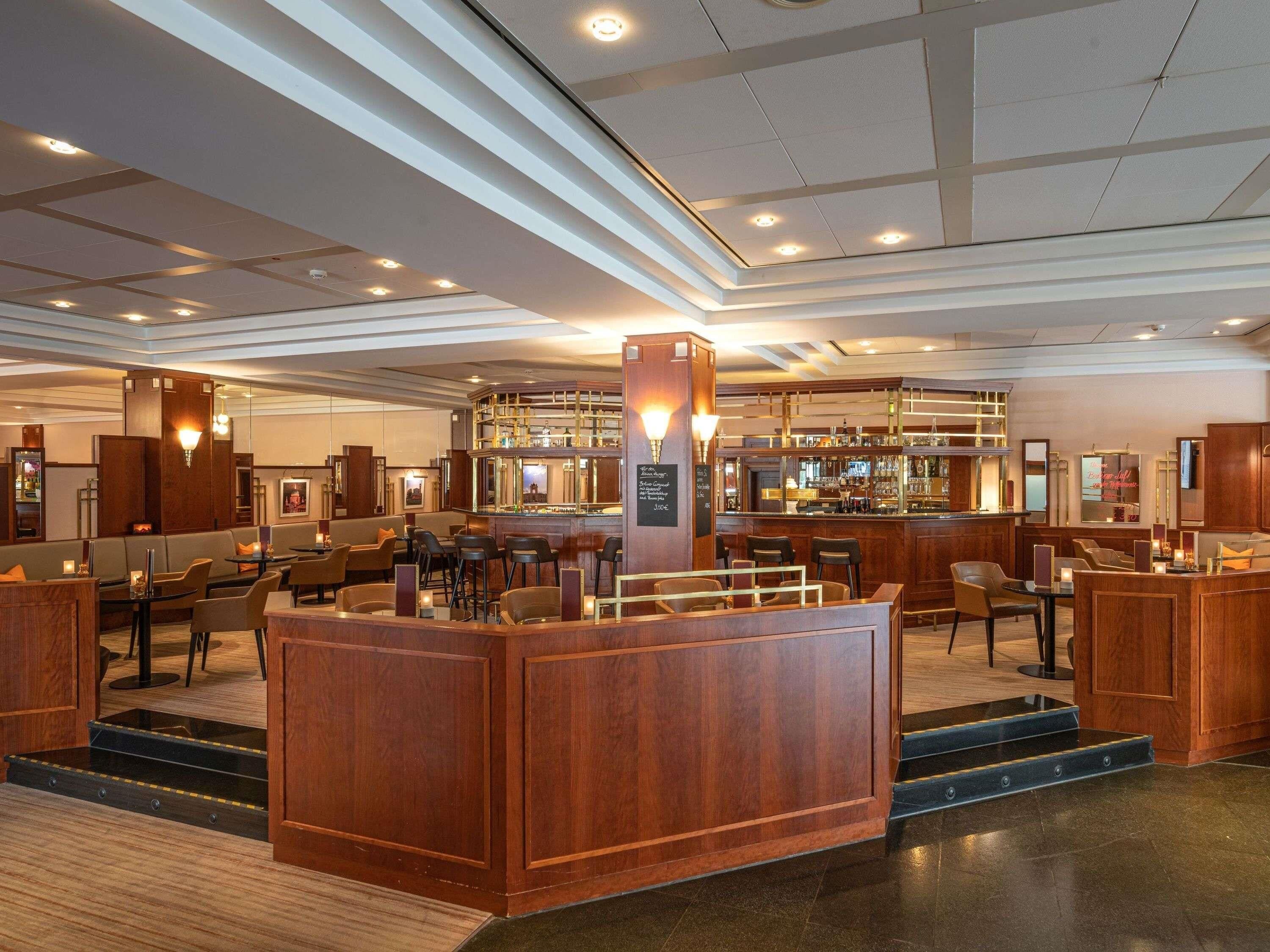 Um saguão de hotel moderno com área de bar, assentos e uma escadaria para outro andar.