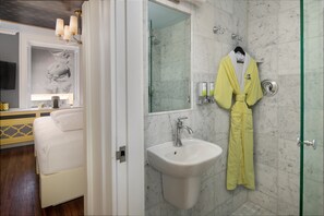Um banheiro de hotel com chuveiro de mármore, pia e roupão amarelo pendurado na parede.