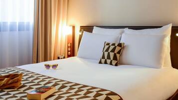 Quarto de hotel com uma cama, manta estampada, um livro e um par de óculos de sol sobre a cama.