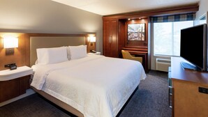 Quarto de hotel com uma cama grande, abajures, uma TV de tela plana, uma escrivaninha com cadeira e uma janela com vista.