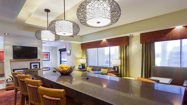 Quarto de hotel moderno com uma grande ilha de cozinha, banquetas de bar e área de estar com sofá e cadeiras.