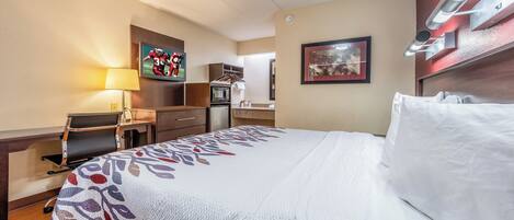 Quarto de hotel com cama, escrivaninha, televisão, micro-ondas e quadro na parede.