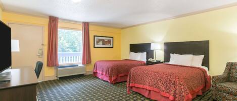 Quarto de hotel com duas camas, uma escrivaninha, uma cadeira, um ventilador de teto e uma janela com cortinas.