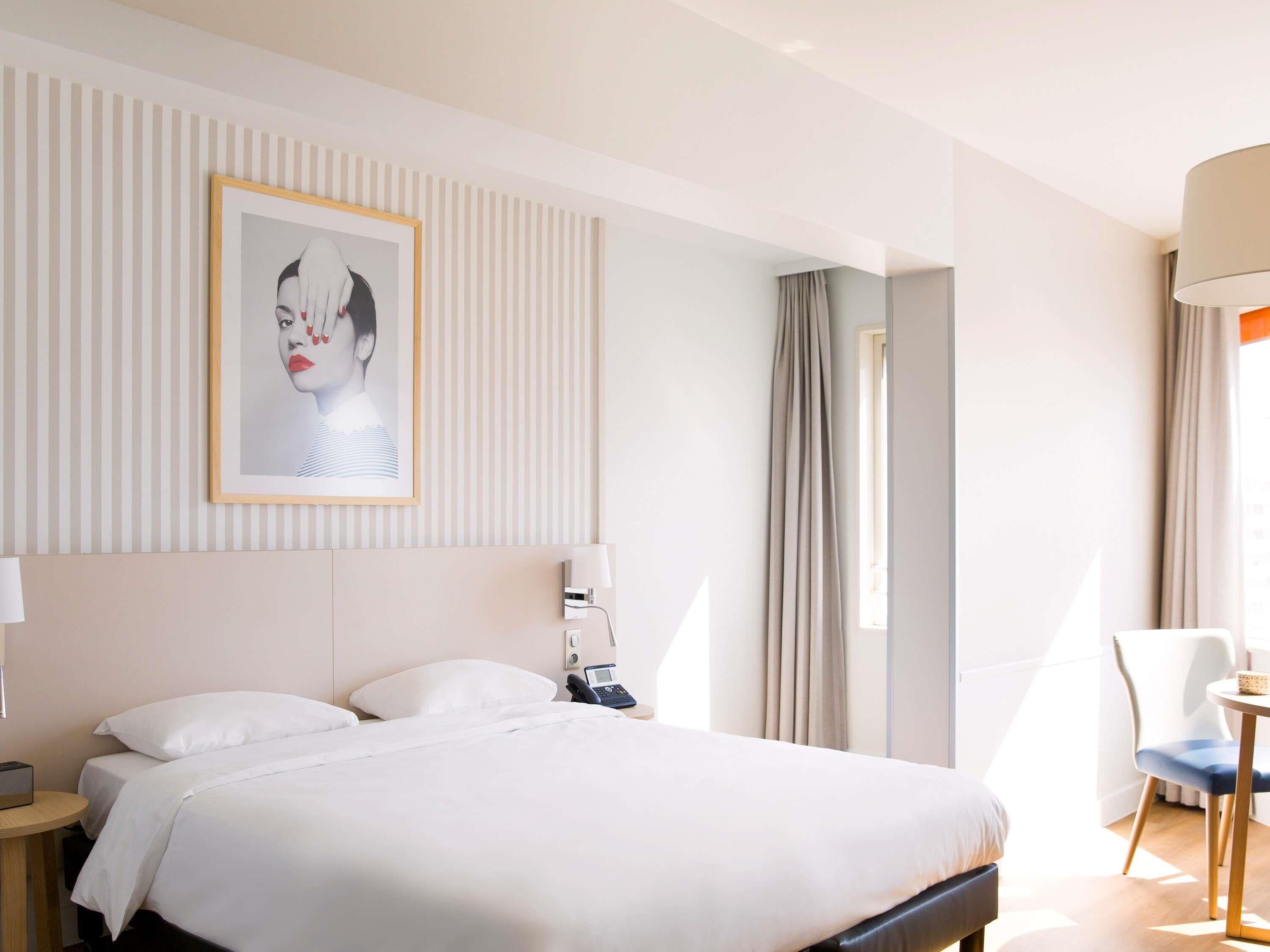 Quarto de hotel com uma cama grande, mesa de cabeceira com abajur, telefone e quadro na parede.