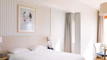 Quarto de hotel com uma cama grande, mesa de cabeceira com abajur, telefone e quadro na parede.