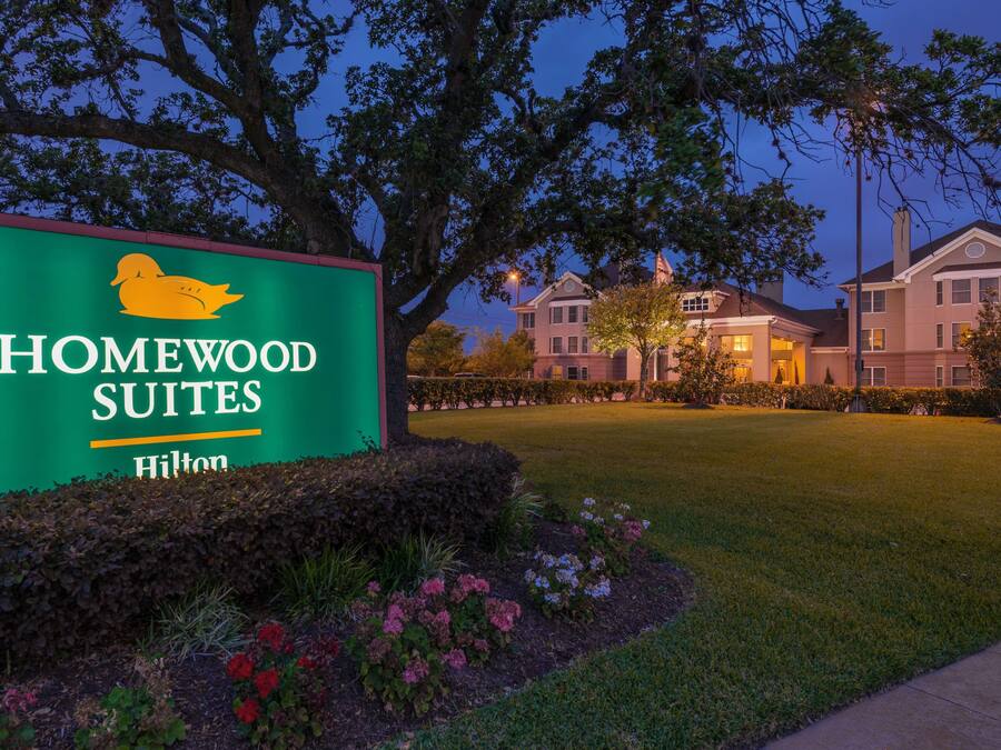 Placa da Homewood Suites by Hilton com uma grande árvore e gramado bem cuidado em primeiro plano.