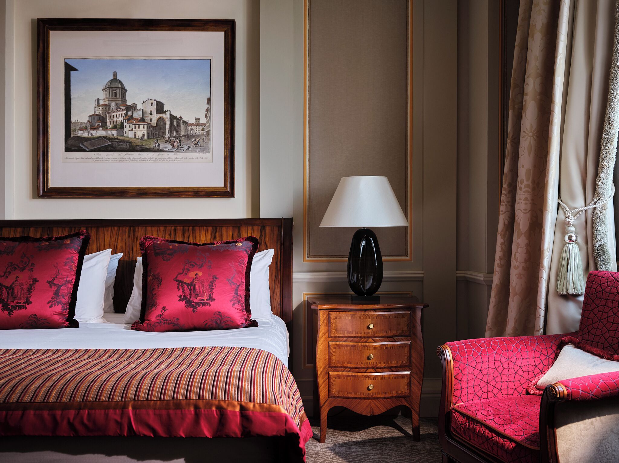 Quarto de hotel com cama, mesa de cabeceira, luminária, cadeira e um quadro na parede.