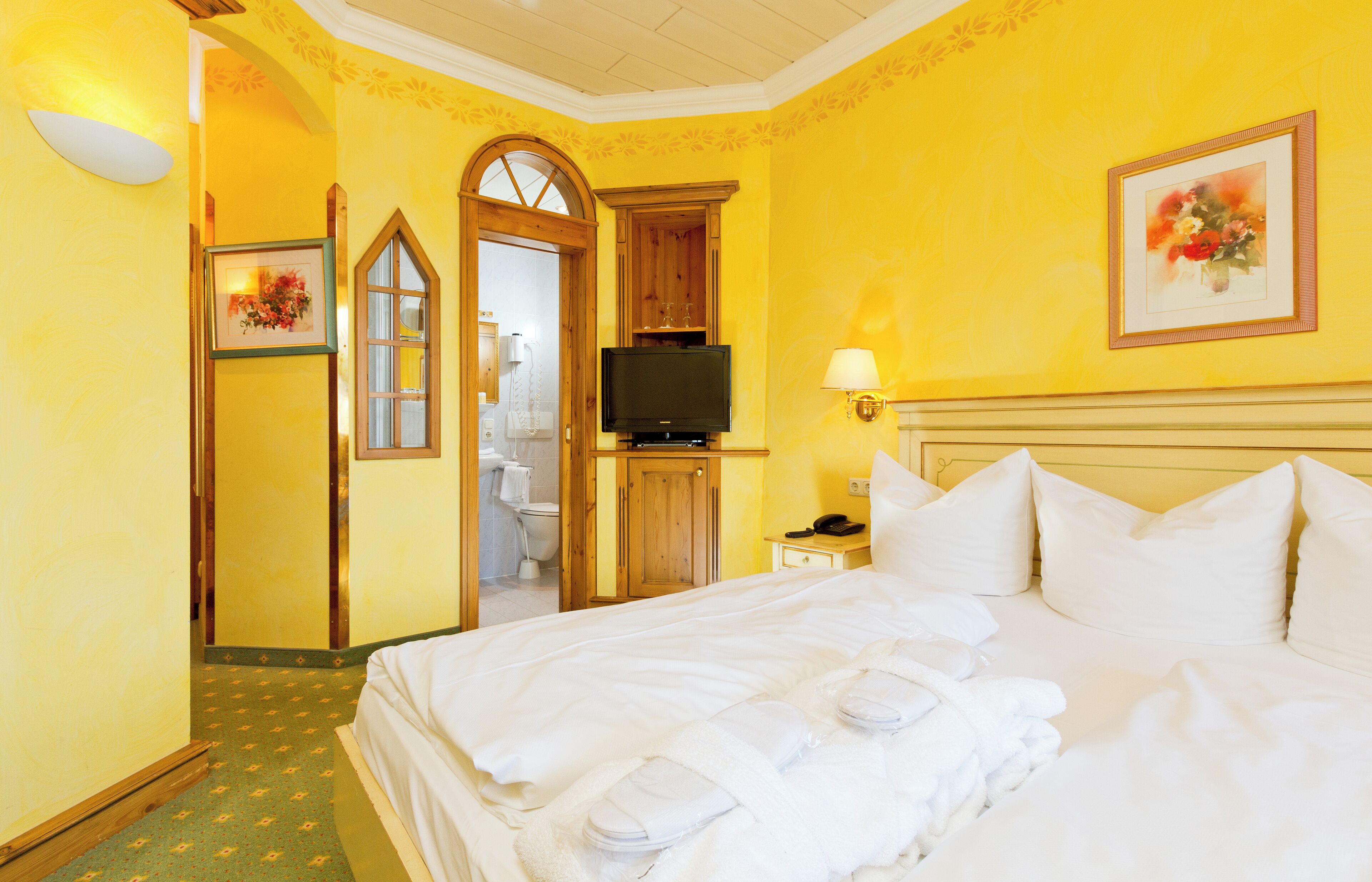 Quarto de hotel com uma cama grande, televisão, luminária e um quadro na parede.