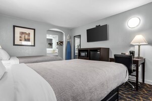 Quarto de hotel com duas camas, uma escrivaninha com computador, televisão e abajur.