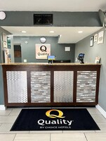 Balcão de recepção de hotel com tela digital, relógio e placa com a inscrição 'Quality by Choice Hotels'.