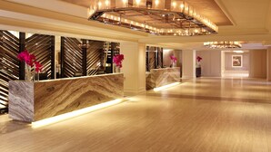 Um hall amplo com balcões de recepção em mármore, um lustre moderno e piso de madeira envernizada.