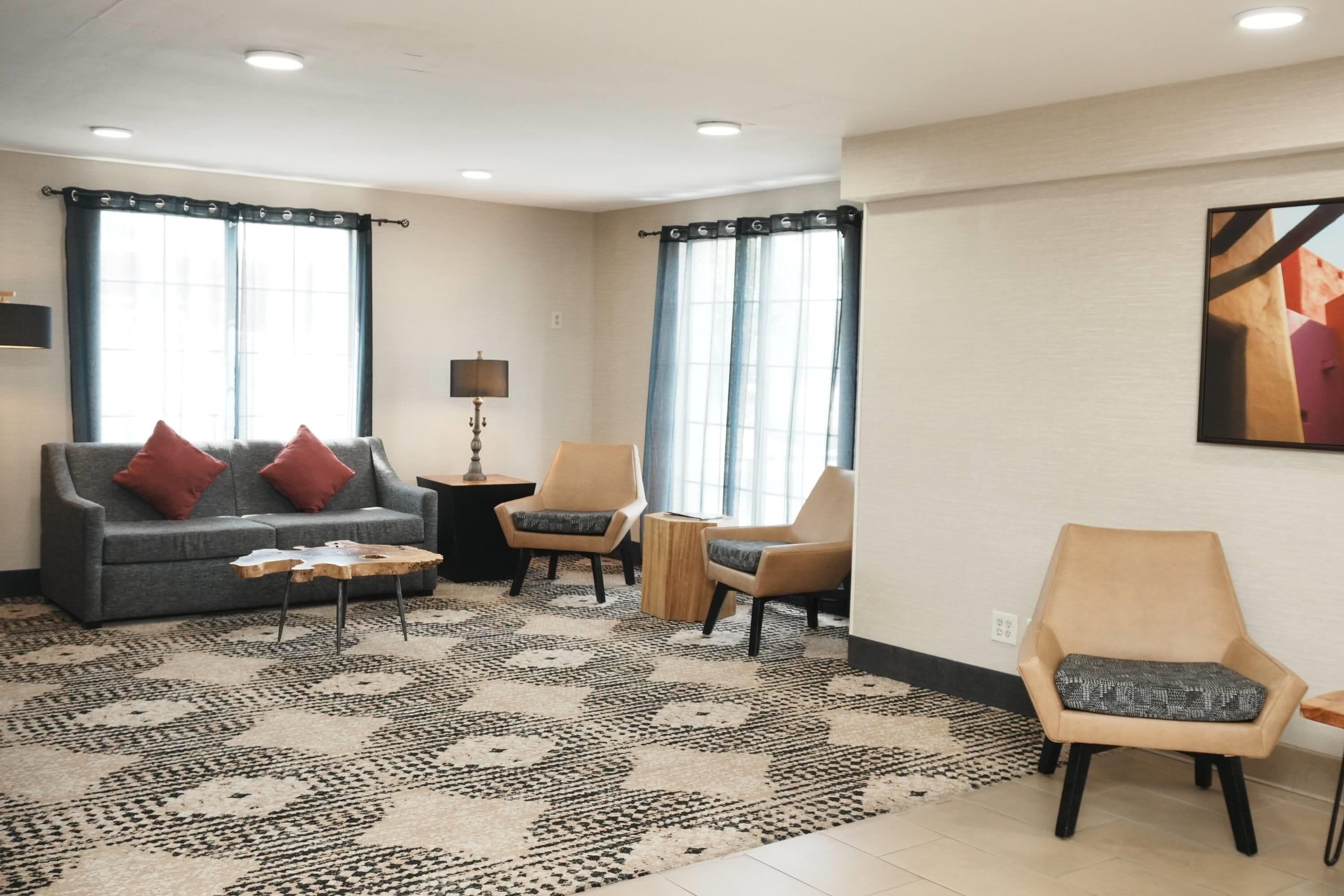 Uma sala de estar com um sofá cinza, duas poltronas, uma mesa de centro e um tapete estampado.