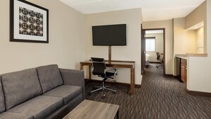 Quarto de hotel com sofá, escrivaninha com cadeira, TV de tela plana e cozinha compacta.