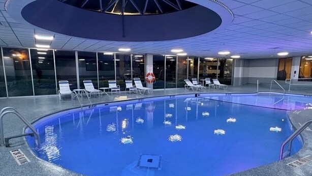 Piscina interna com água cristalina, cercada por espreguiçadeiras e um painel de vidro.